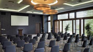 Uma sala de conferências com fileiras de cadeiras, um pódio e uma tela grande.