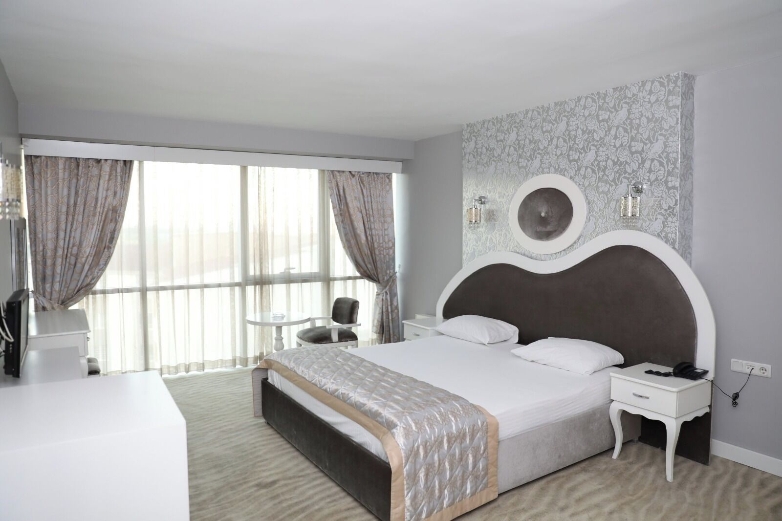 Quarto de hotel com uma cama grande, mesa de cabeceira, uma cadeira e uma escrivaninha.