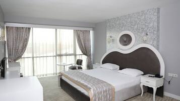Quarto de hotel com uma cama grande, mesa de cabeceira, uma cadeira e uma escrivaninha.
