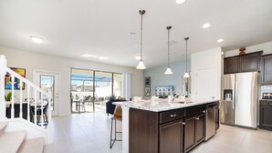 Uma cozinha espaçosa com armários escuros, uma ilha grande, eletrodomésticos de aço inoxidável e iluminação pendente.