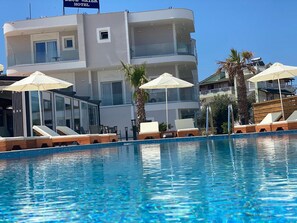 Um hotel com área de piscina, cadeiras de sol e guarda-sóis.