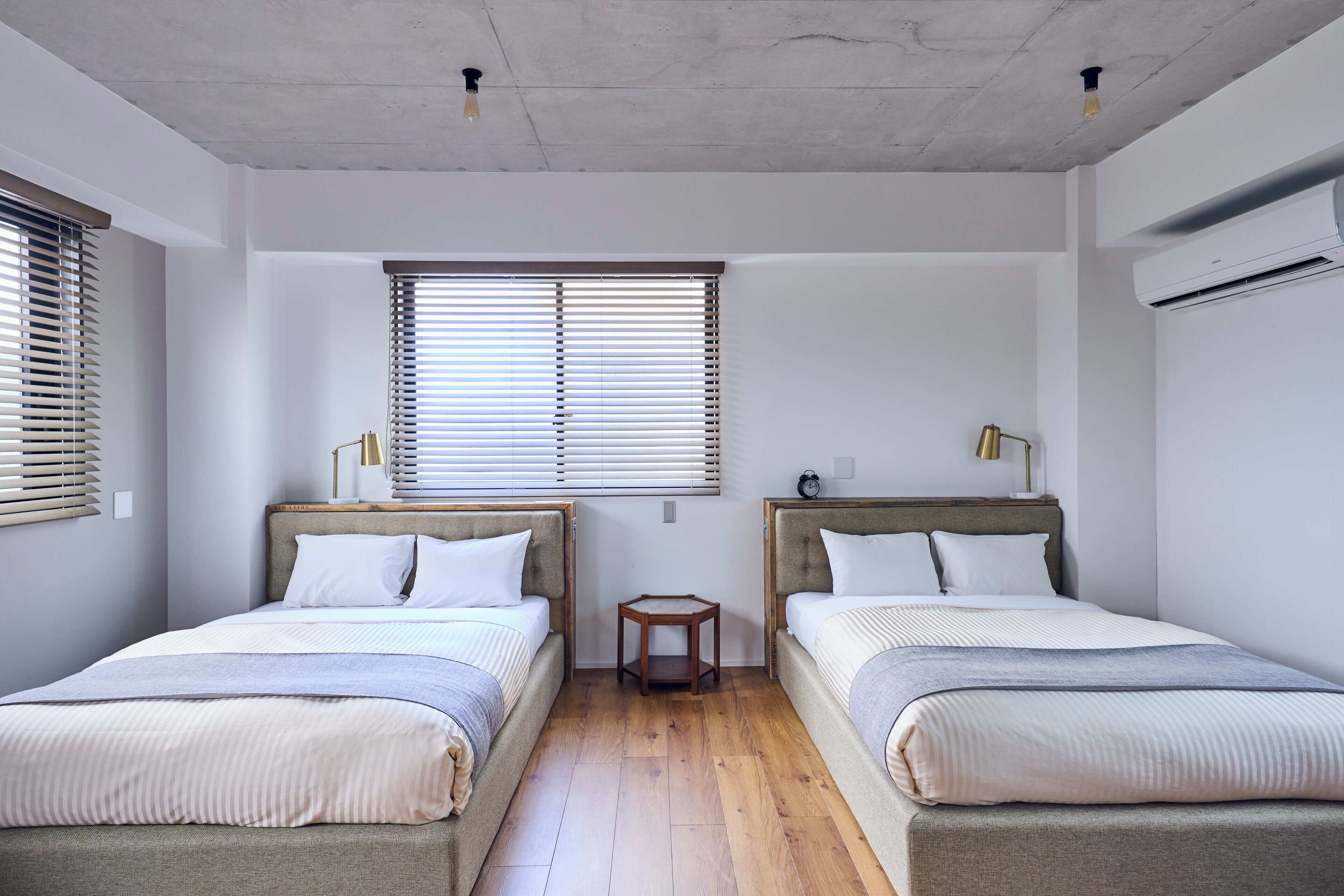 Quarto com duas camas, uma mesinha e aparelho de ar condicionado.