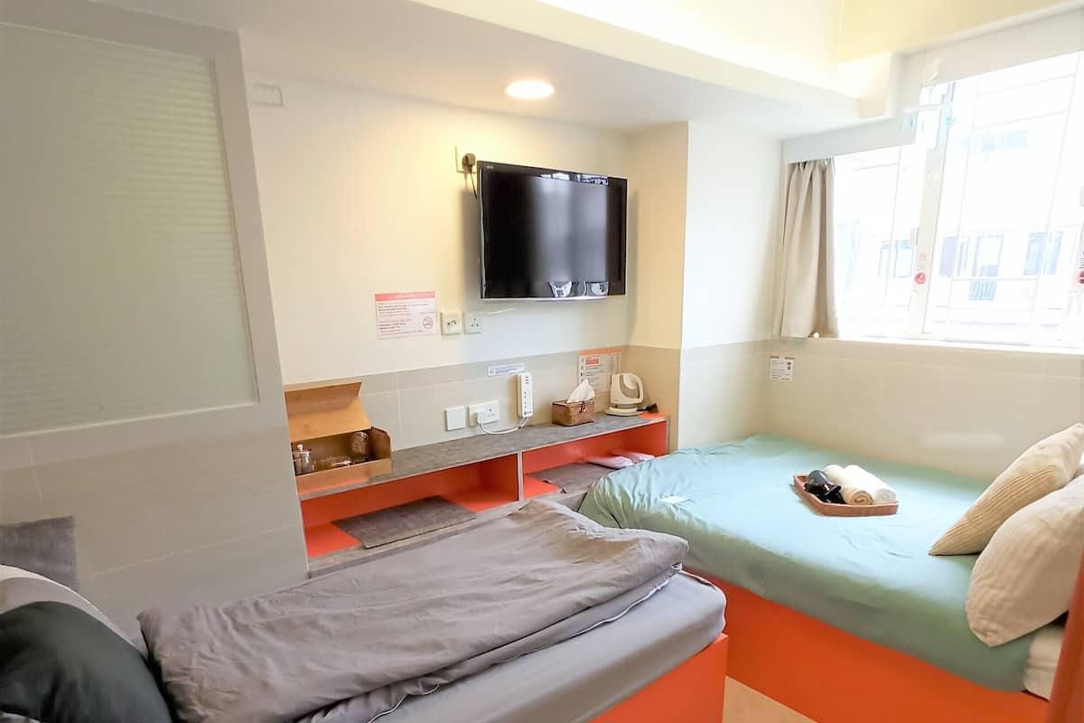 Quarto de hotel compacto com uma cama, televisão, mesa pequena e janela.