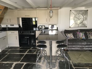 Uma cozinha moderna com uma ilha central, banquetas de bar, um relógio grande e um sofá com almofadas estampadas.