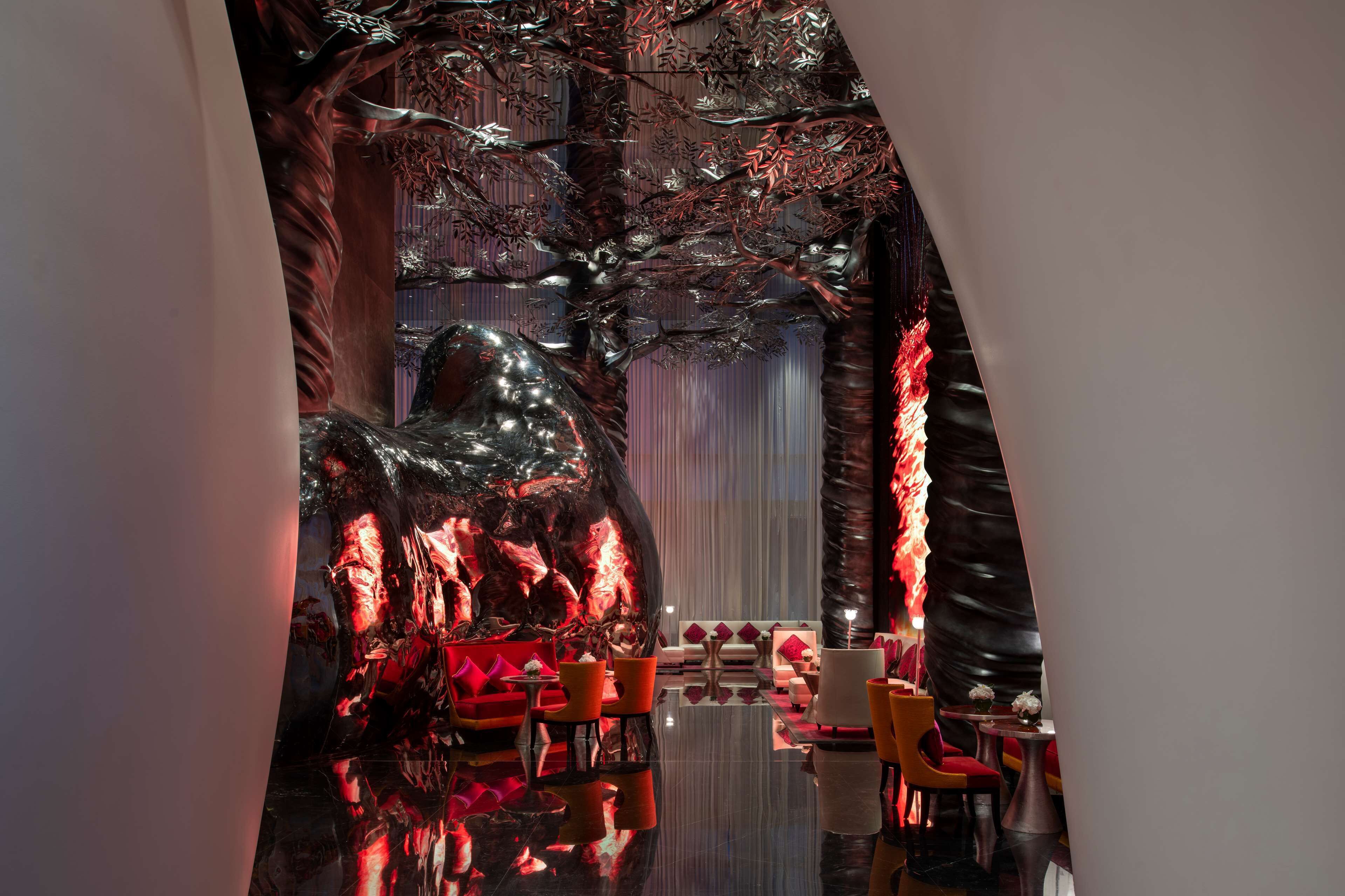 Interior moderno com piso refletivo, assentos em vermelho e branco, e uma estrutura de árvore decorativa no centro.