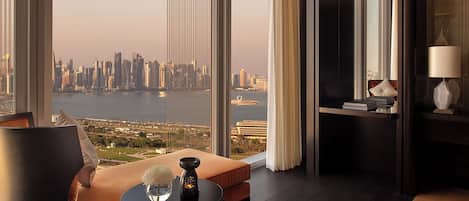 Quarto de hotel moderno com uma grande janela que oferece vista para a cidade, um espaço de estar confortável e uma pequena mesa com objetos decorativos.