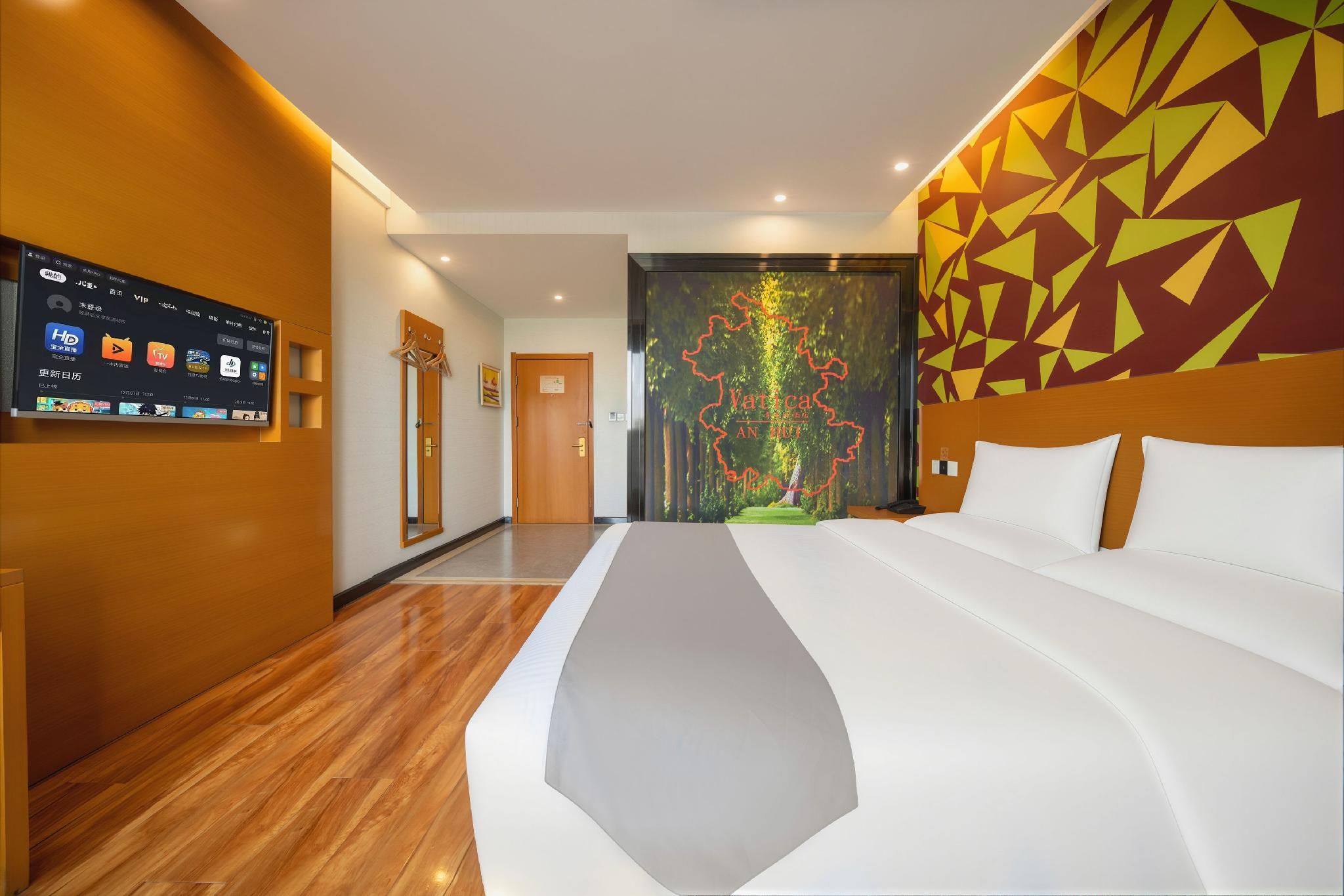 Quarto de hotel com uma cama grande, uma tela digital na parede e um design geométrico na parede.