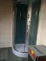 Divisória de chuveiro com paredes de vidro, chão em azulejo branco e uma geladeira Red Bull no canto.
