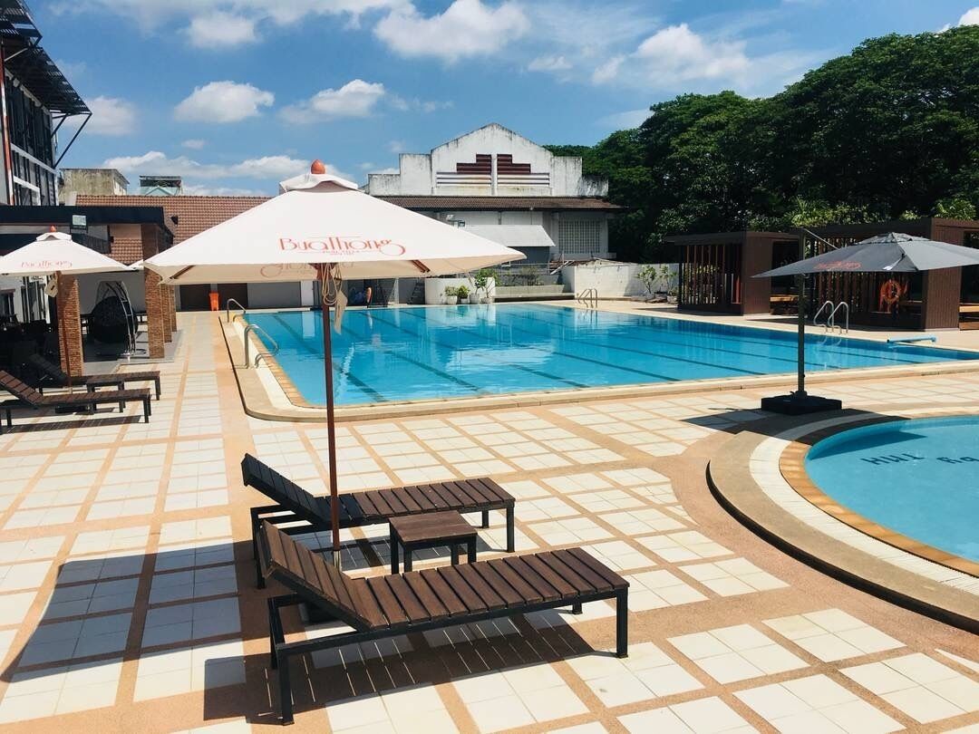 Área de piscina com espreguiçadeiras e guarda-sóis, ladeada por um deck revestido em azulejo.