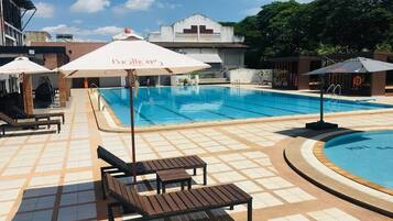 Área de piscina com espreguiçadeiras e guarda-sóis, ladeada por um deck revestido em azulejo.