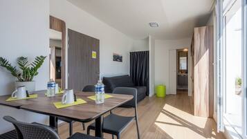 Quarto de hotel moderno com uma mesa de jantar de madeira, cadeiras pretas, um sofá e uma janela grande.