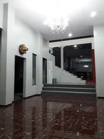 Um interior moderno com piso de mármore, um candelabro e uma escadaria que leva a um cômodo escuro.