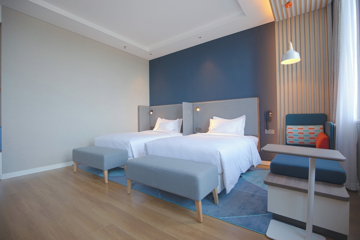 Quarto de hotel com duas camas, uma escrivaninha e uma cadeira.