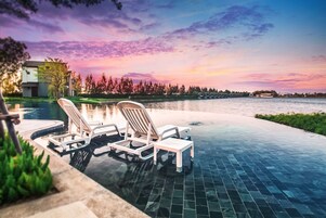 Uma piscina infinita com espreguiçadeiras, vista clara da água e um céu ao pôr do sol.