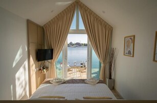 Quarto com cama grande, TV e vista para a água através de janela com cortinas.