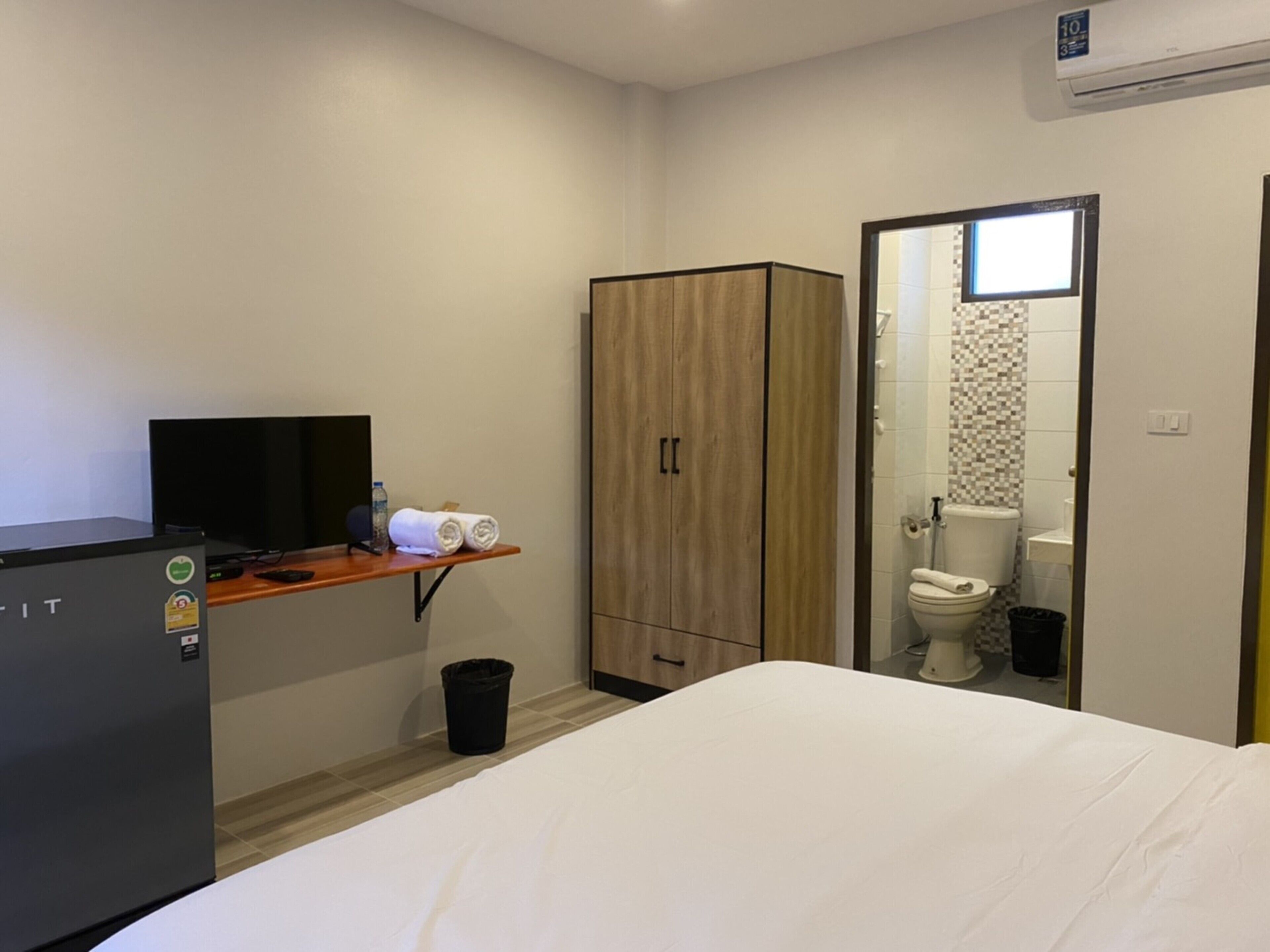 Quarto de hotel com uma cama, televisão, guarda-roupa e banheiro visível por uma porta aberta.