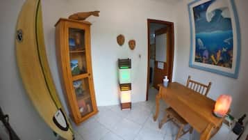 Quarto com armário de madeira, uma prancha de surf, mesa com cadeira, aquecedor fixado na parede e um quadro emoldurado.