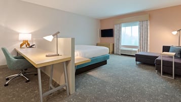 Quarto de hotel com cama, escrivaninha com luminária, poltrona, sofá, televisão e janela com cortinas.