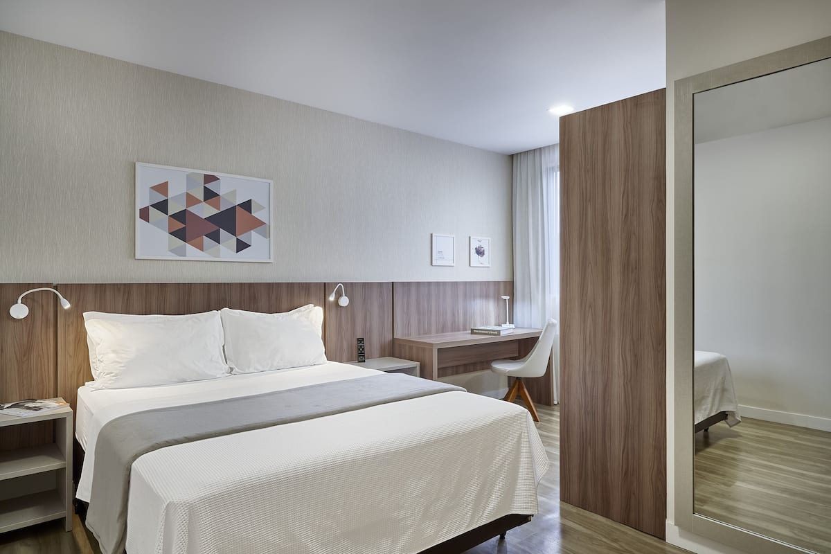Quarto de hotel moderno com uma cama grande, uma escrivaninha e uma cadeira.