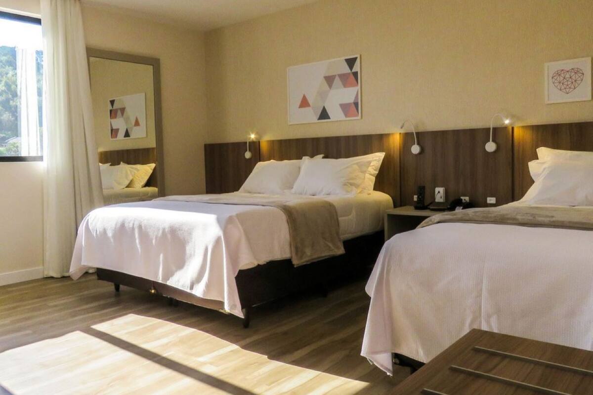 Quarto de hotel com duas camas, piso de madeira e obras de arte nas paredes.