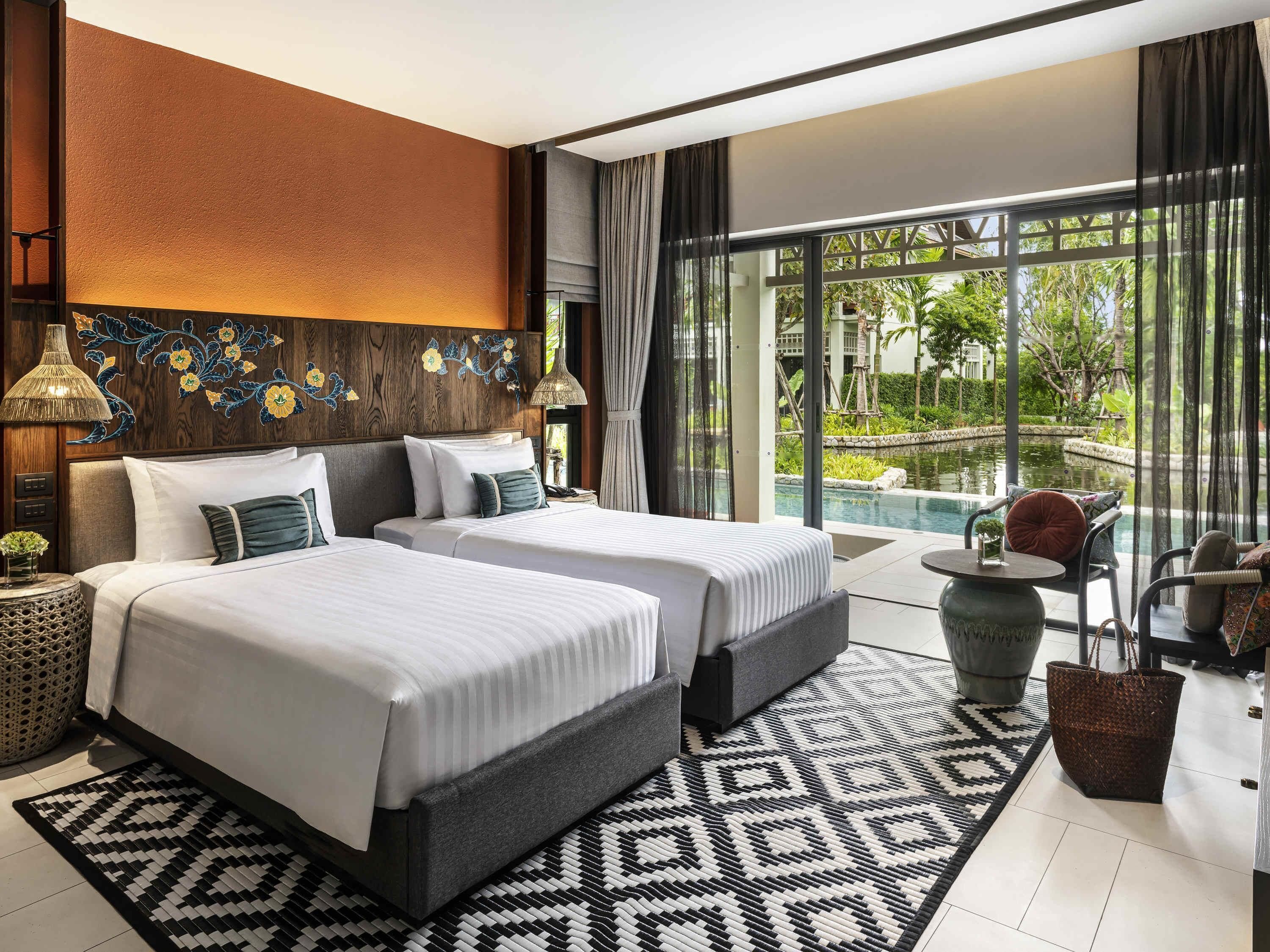Quarto de hotel com duas camas, uma janela grande com vista para uma piscina, um tapete tecido e um painel decorativo na parede.