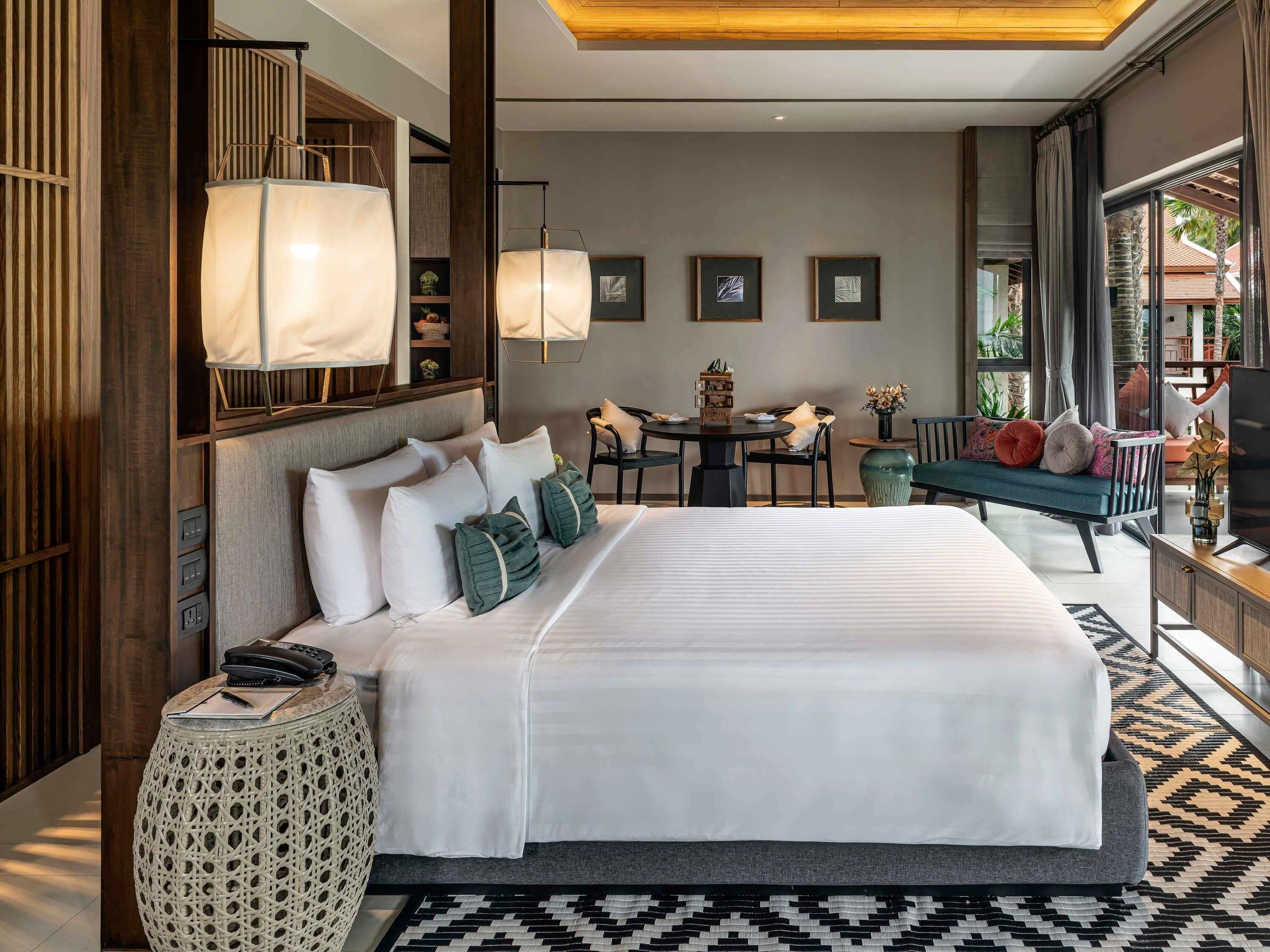 Quarto de hotel com uma cama grande, luminárias de cabeceira, uma mesa redonda e um sofá.