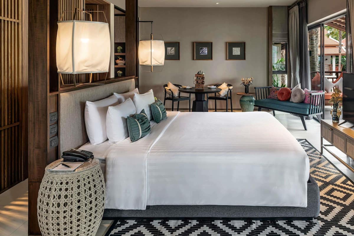 Quarto de hotel com uma cama grande, luminárias de cabeceira, uma mesa redonda e um sofá.