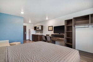 Quarto de hotel com cama, escrivaninha, cadeira, televisão e guarda-roupa.