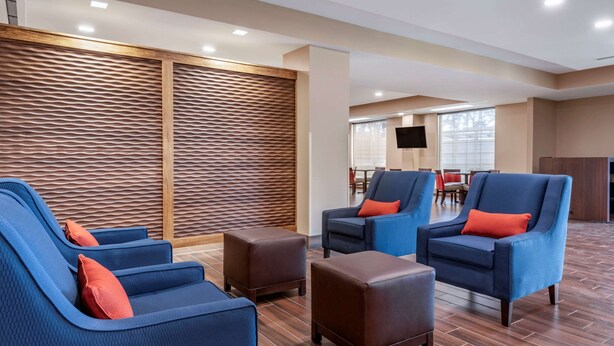 Um lobby moderno com poltronas azuis, pufes marrons e uma parede de madeira texturizada.