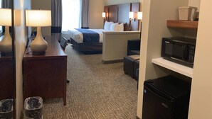 Quarto de hotel com uma cama, uma escrivaninha com luminária, micro-ondas e lixeira.
