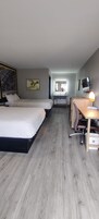 Quarto de hotel com duas camas, uma escrivaninha, uma cadeira, uma televisão e uma janela.