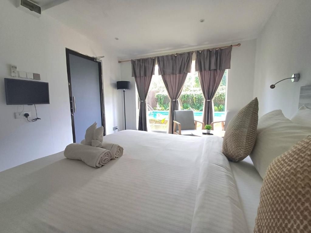 Quarto de hotel com uma cama grande, televisão de tela plana na parede e vista para uma piscina e área externa com assentos.