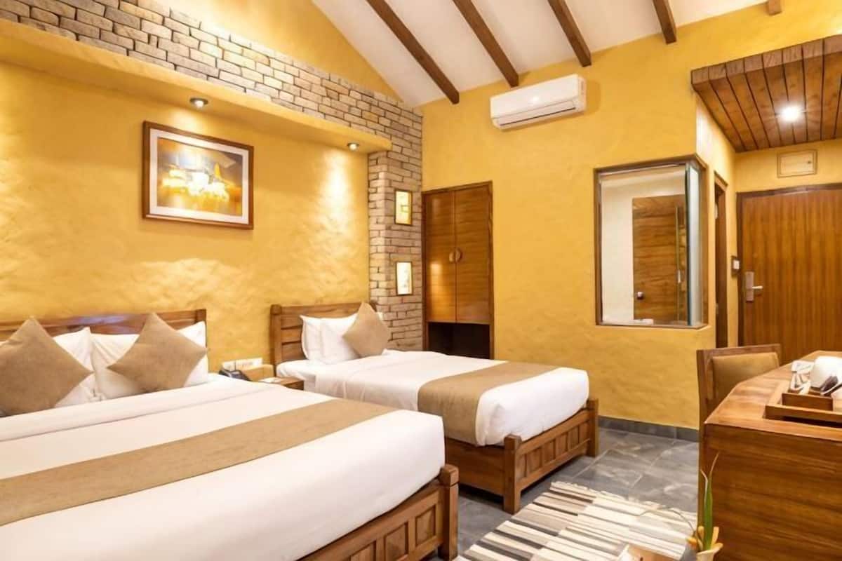 Quarto de hotel com duas camas, uma escrivaninha de madeira, um espelho e uma parede de tijolos.