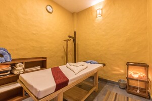 Um quarto com uma mesa de massagem de madeira, um relógio na parede e uma pequena prateleira com toalhas.
