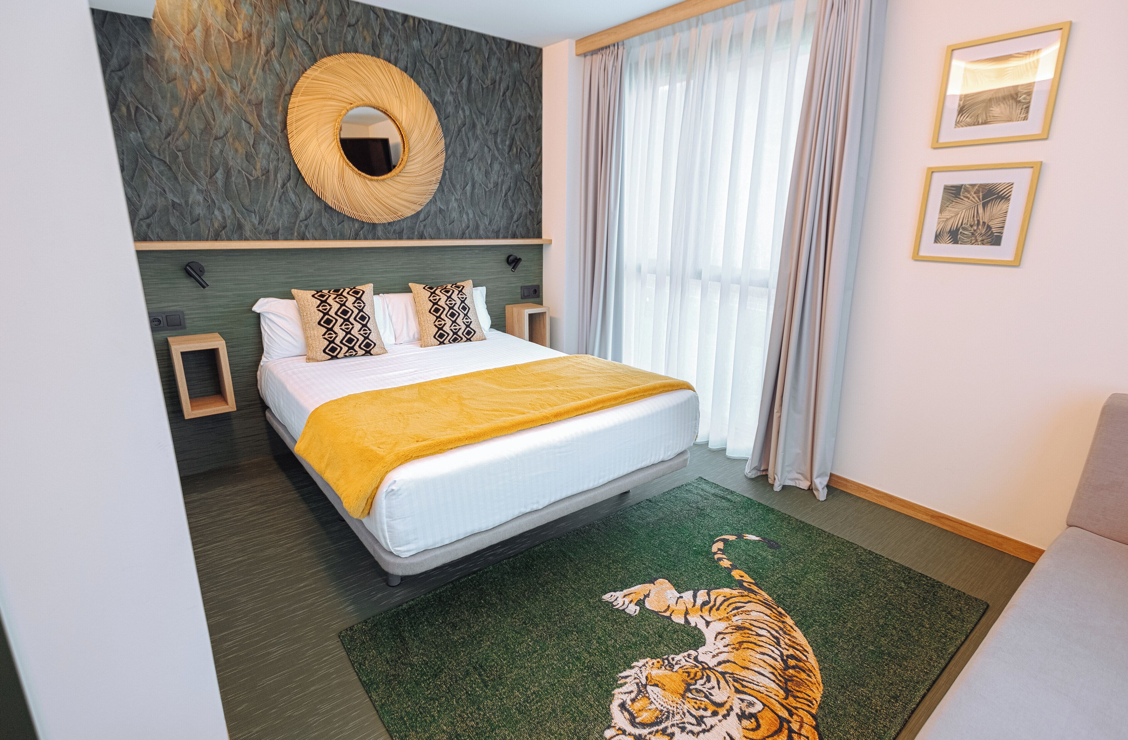 Quarto de hotel moderno com uma cama grande, um espelho redondo, um tapete de tigre e vista para o exterior através de cortinas translúcidas.