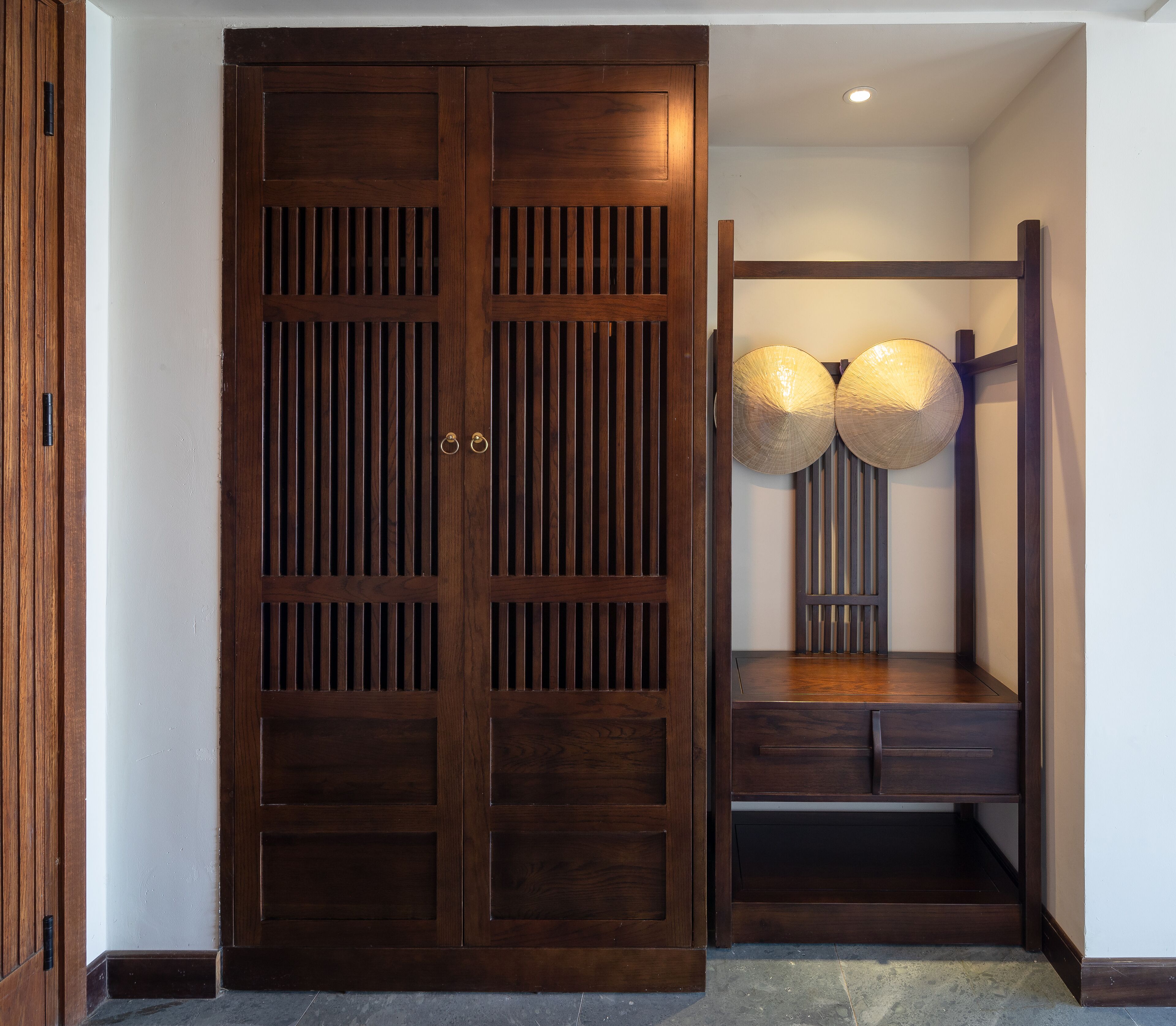 Um guarda-roupa de madeira com duas portas, uma pequena prateleira e uma luminária pendente.