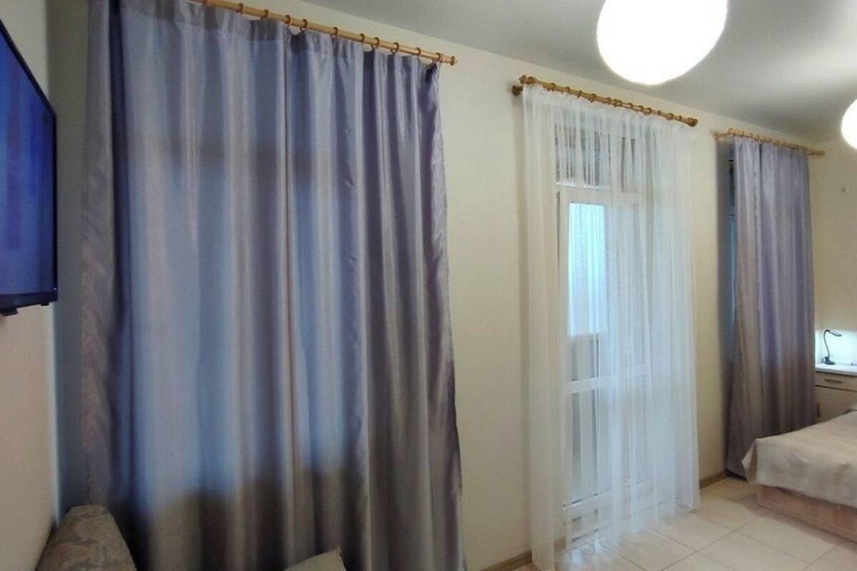 Quarto com cama, cortinas, televisão e janela.
