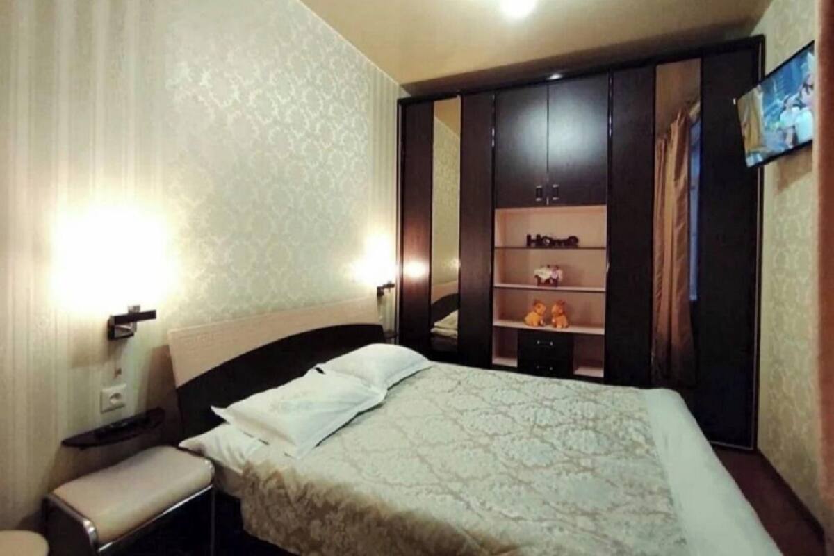 Quarto de hotel com uma cama, um banco, um guarda-roupa e uma televisão.