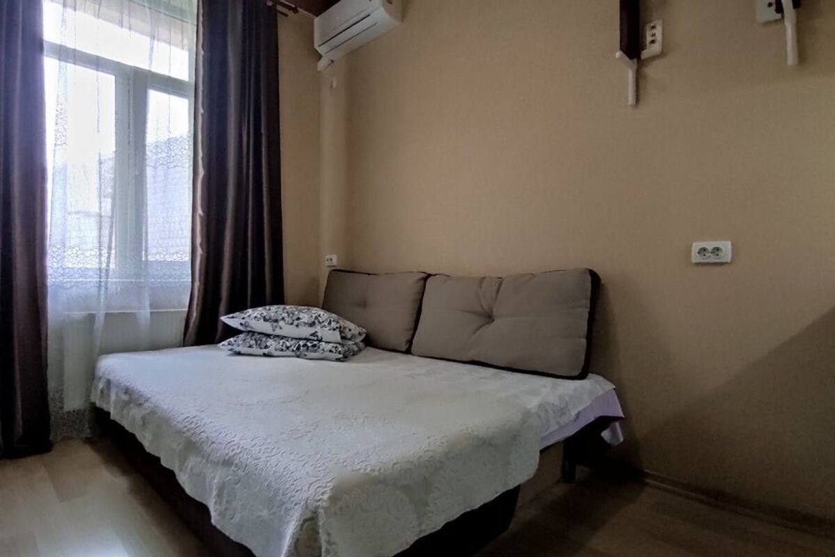 Quarto com cama, janela com cortinas, ar-condicionado e tomada na parede.