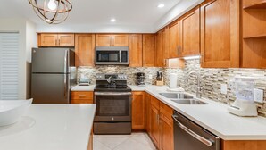 Uma cozinha moderna com armários de madeira, eletrodomésticos de aço inoxidável, painel de azulejos e bancada branca.