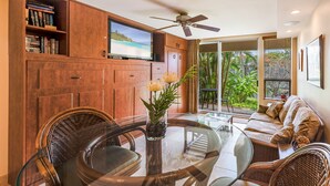 Uma sala de estar moderna com uma mesa de vidro, cadeiras de vime, um sofá e uma televisão sobre um armário de madeira.