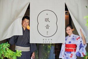 Entrada de um hotel com uma placa exibindo caracteres japoneses e o nome "NEON HOTEL".