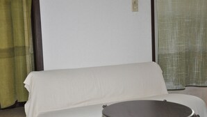 Um quarto com um sofá branco, uma mesa redonda e uma janela com cortinas verdes.