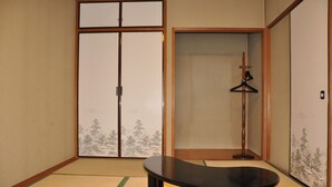 Um quarto japonês tradicional com tatames, uma mesa preta, portas corrediças com cena da natureza e um cabide de roupas.