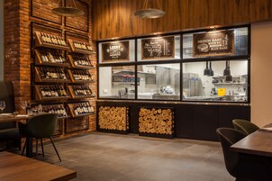 Interior de restaurante com paredes de madeira, prateleiras de vinho e cozinha visível através de uma divisória de vidro.