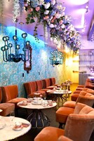 Restaurante com mesas redondas, cadeiras estofadas em laranja e decorações florais penduradas.