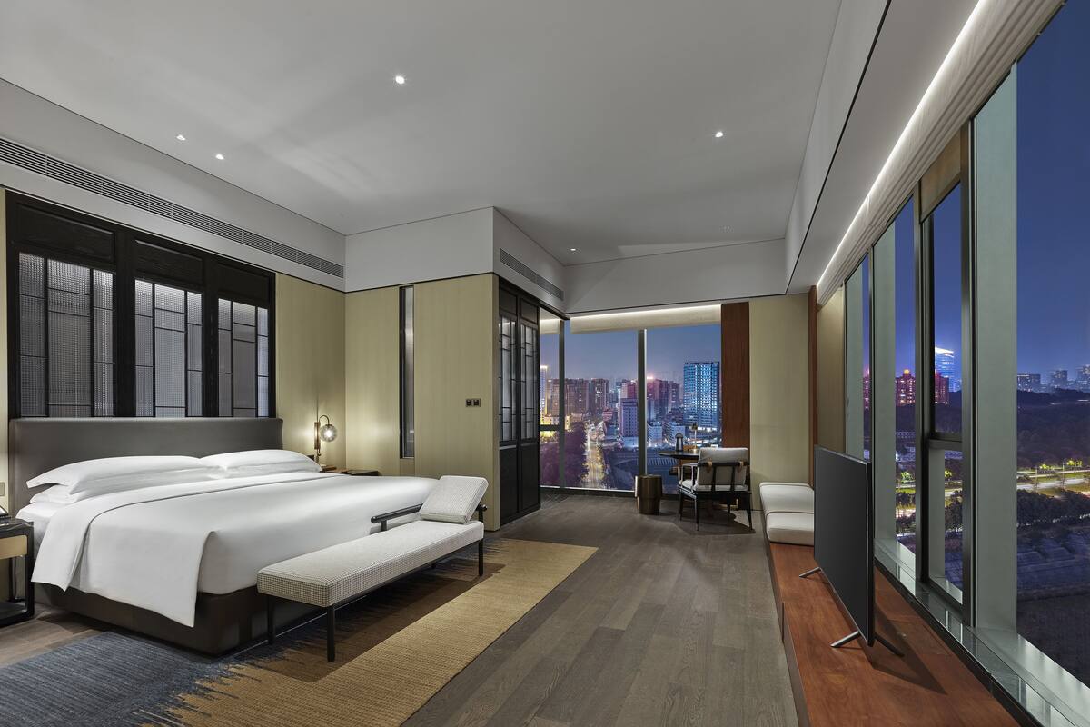 Quarto de hotel moderno com cama grande, área de estar e vista para a cidade.
