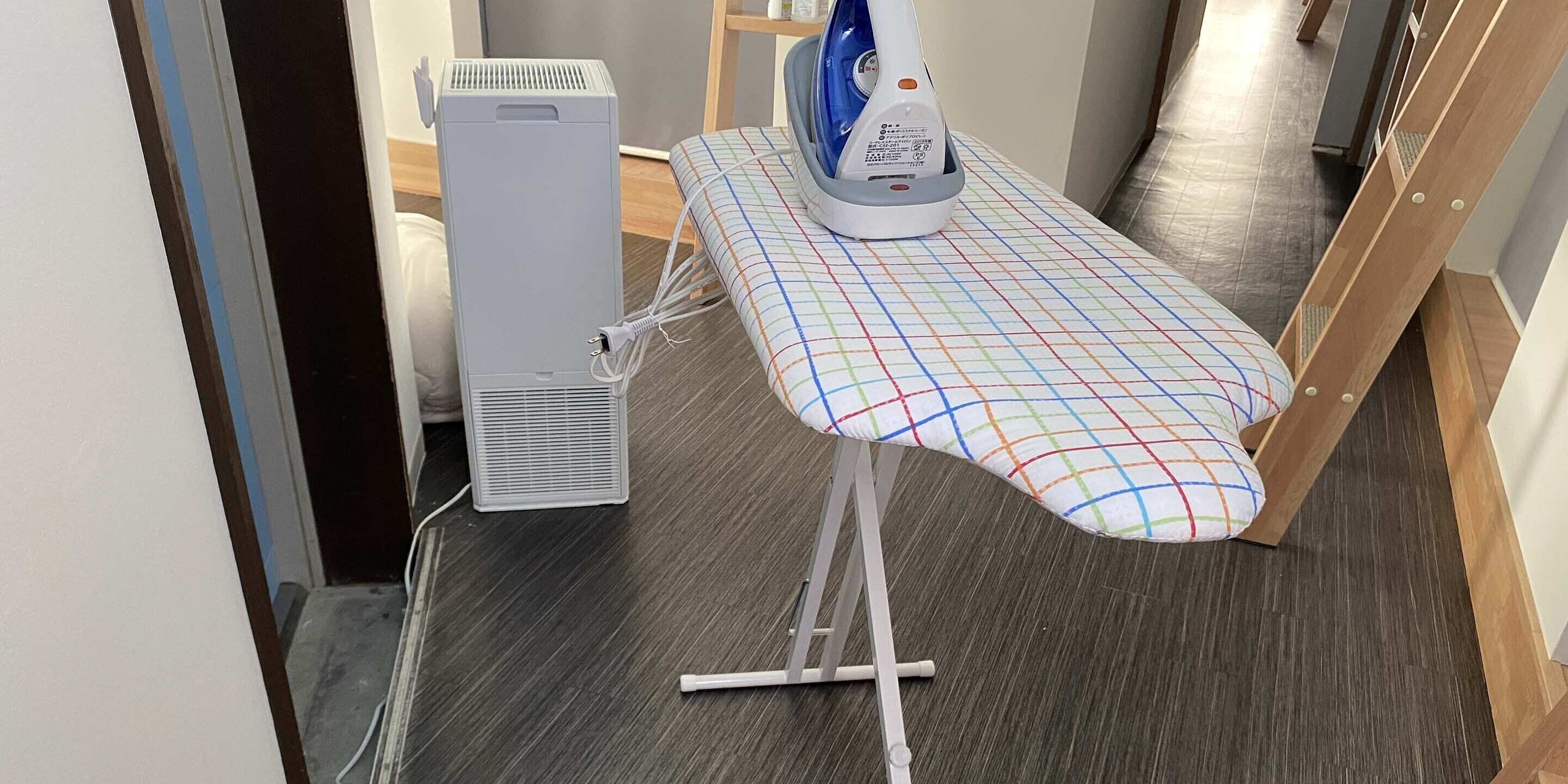 Quarto compacto com um espaço pequeno para passar roupa, um radiador branco e piso de madeira.