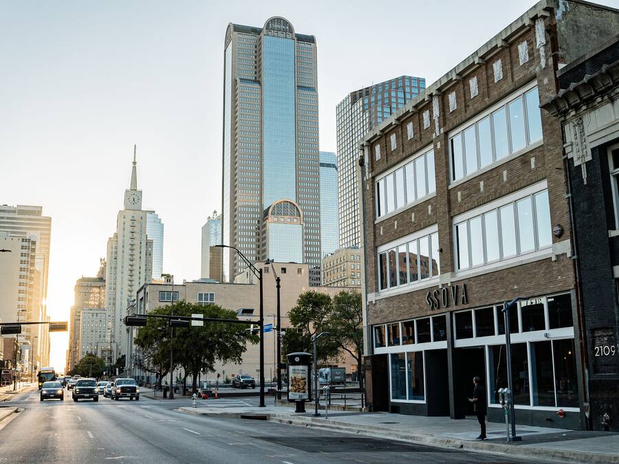 Uma rua urbana com prédios altos, incluindo um arranha-céu imponente.