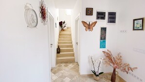 Um corredor com uma escada, um relógio e diversas decorações nas paredes, incluindo uma borboleta, quadros e um vaso com flores.